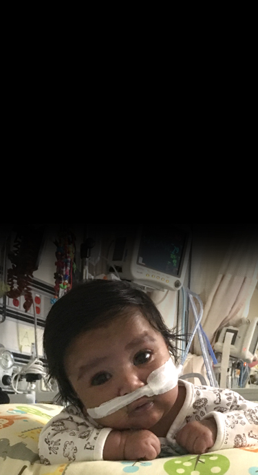 Maxen in treatment at SickKids on his front looking at the camera